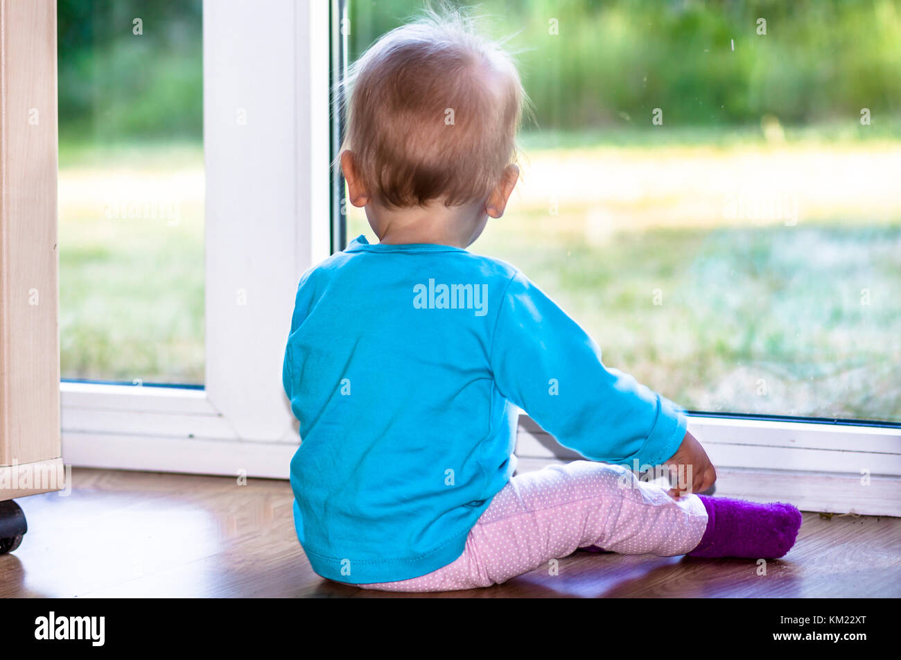 View form behind of toddler sitting in front of a big window with the ...