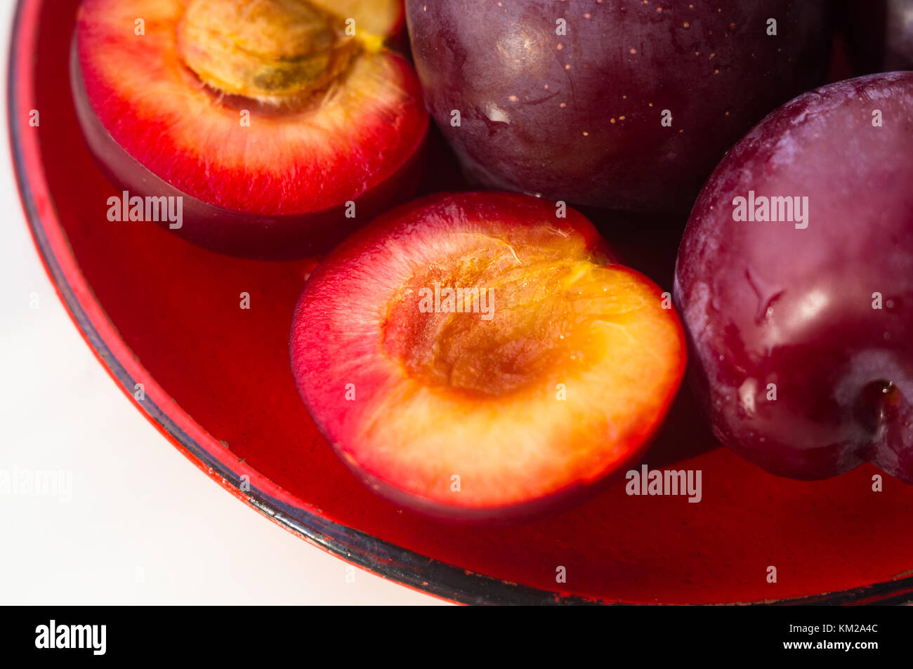 fresh plum fruit with cut plum slices in the red saucer on white ...