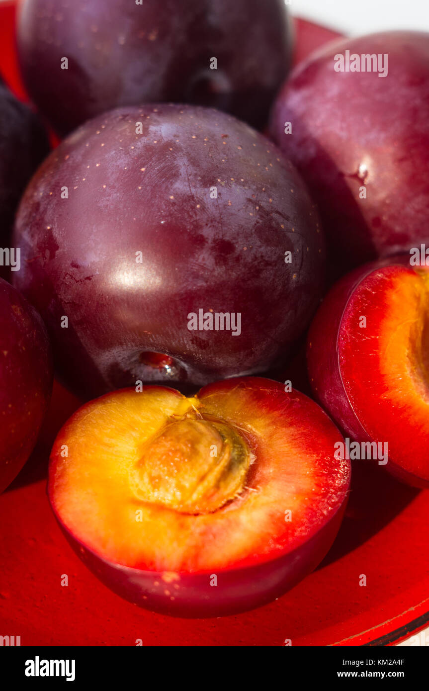 fresh plum fruit with cut plum slices in the red saucer on white ...
