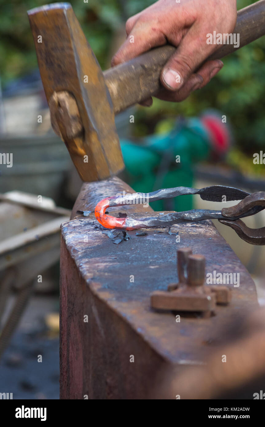 blacksmith performs the forging of hot glowing metal on the anvil ...