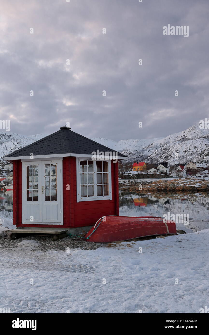 Red painted rowboat and wooden cabin with black roof and white closed ...