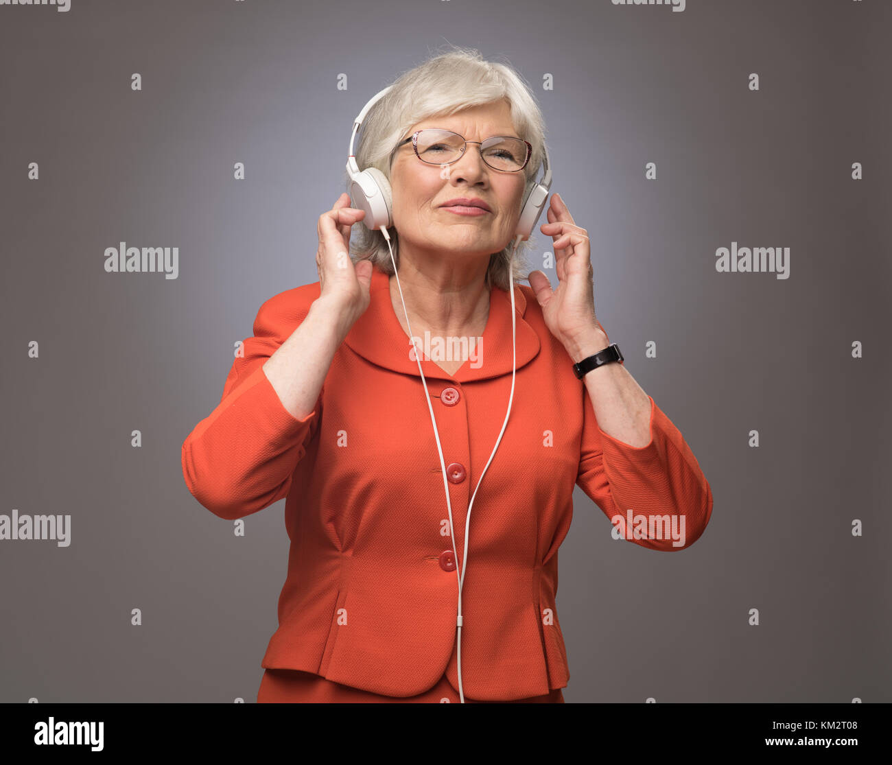 Smiling senior lady with headphones on listening to the music on gray ...