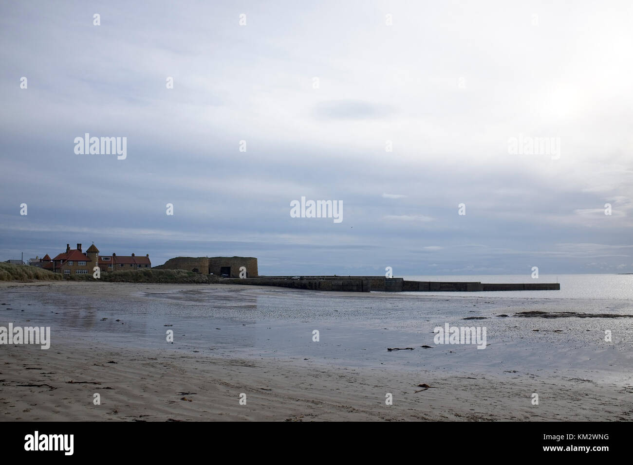 Beadnell Bay harbour walls and lime kilns seen across sandy beaches ...