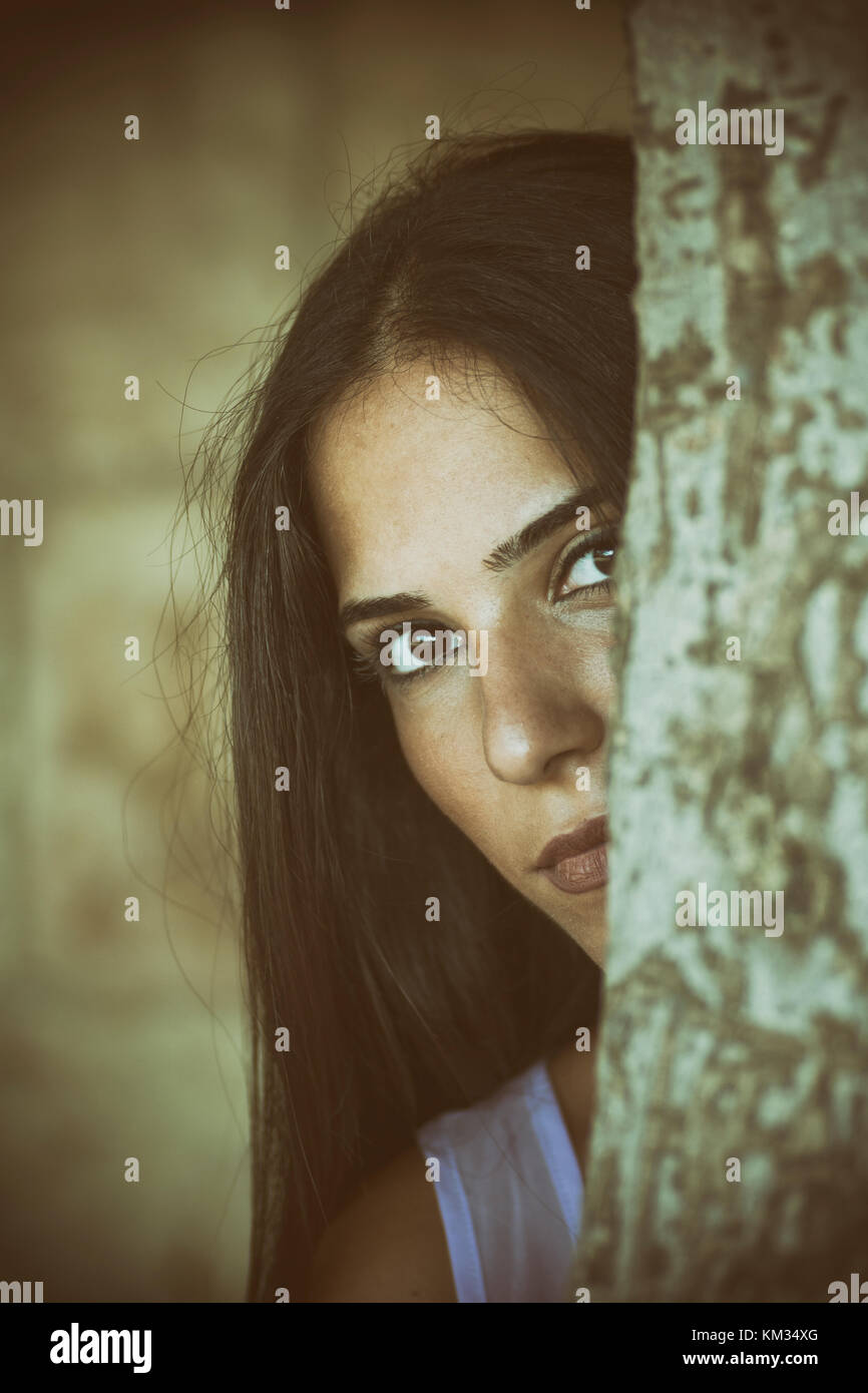 Beautiful young woman standing behind a tree Stock Photo - Alamy