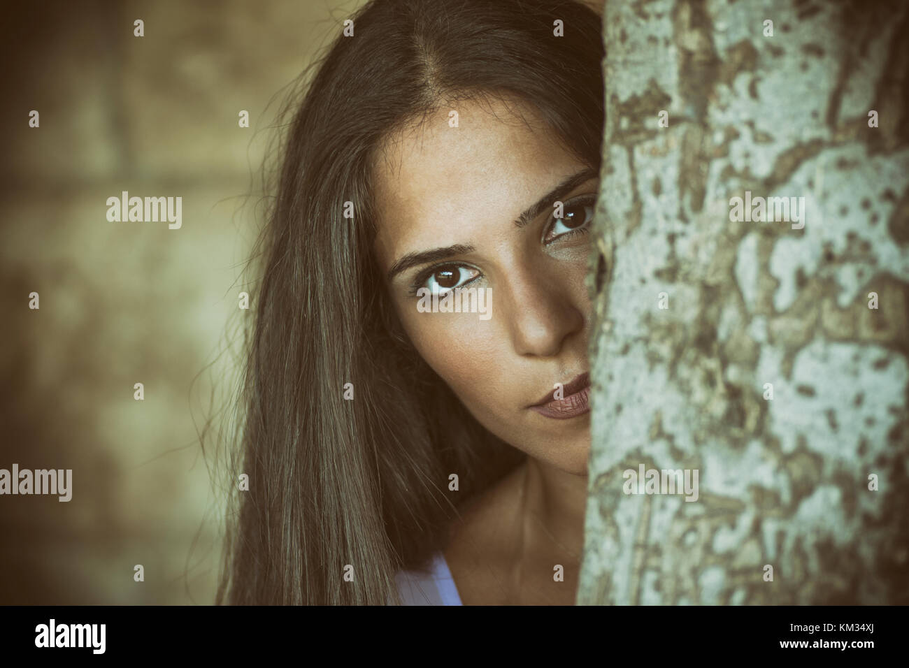 Beautiful young woman standing behind a tree Stock Photo - Alamy