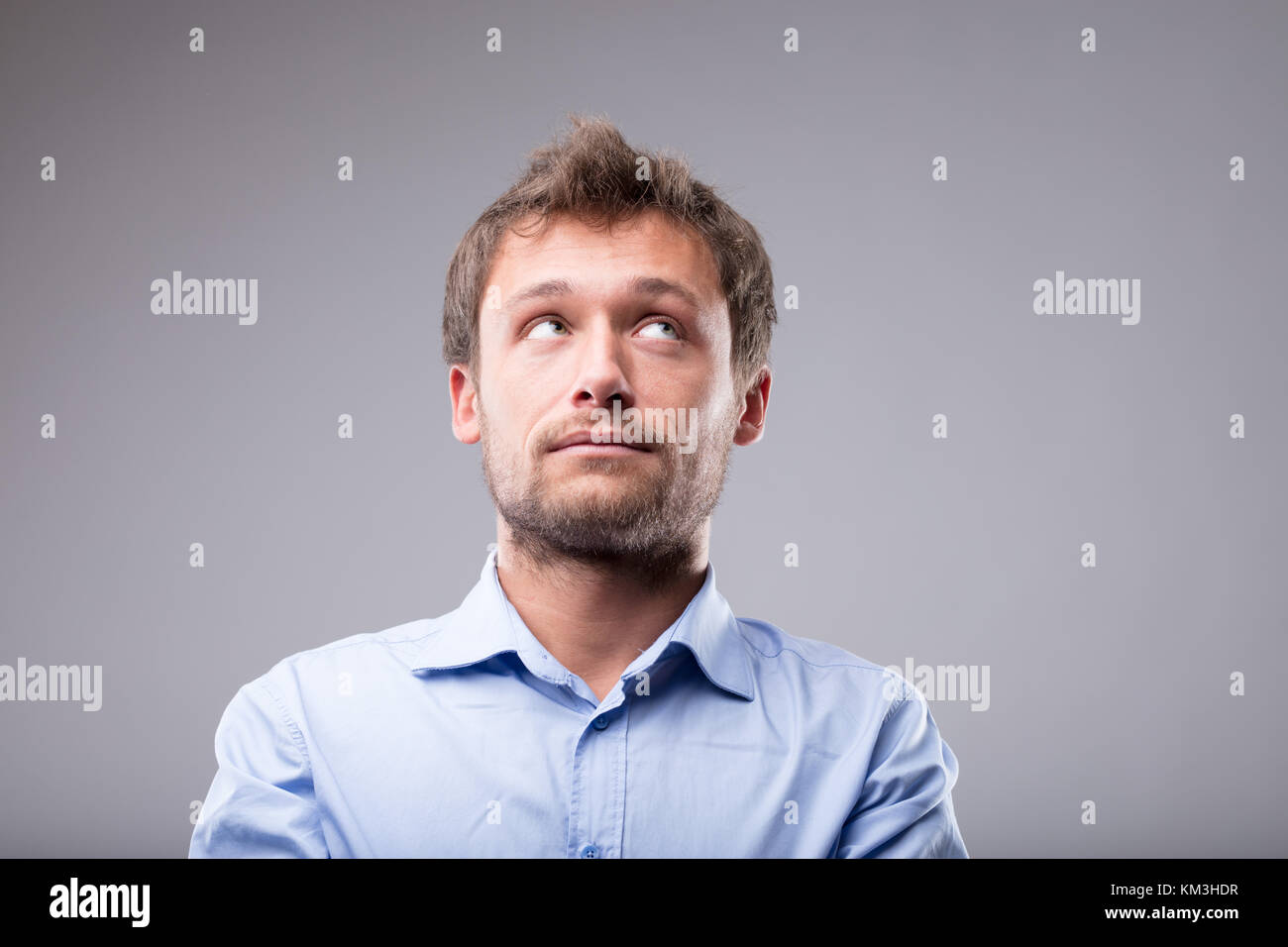 Thoughtful young man standing daydreaming looking up into the air with ...