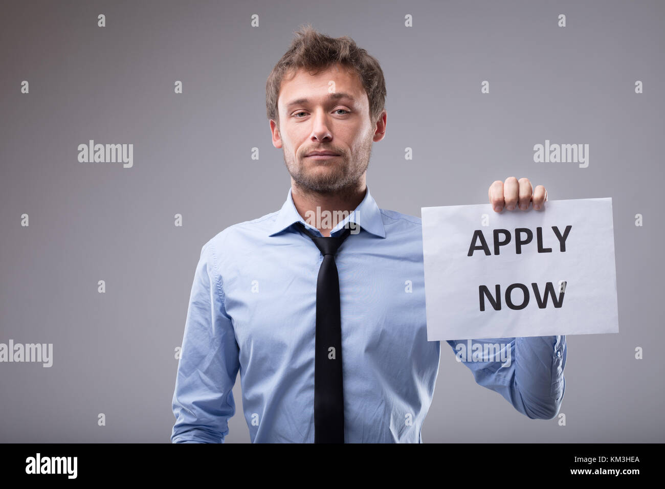 Young businessman holding up an Apply Now sign looking at the camera ...