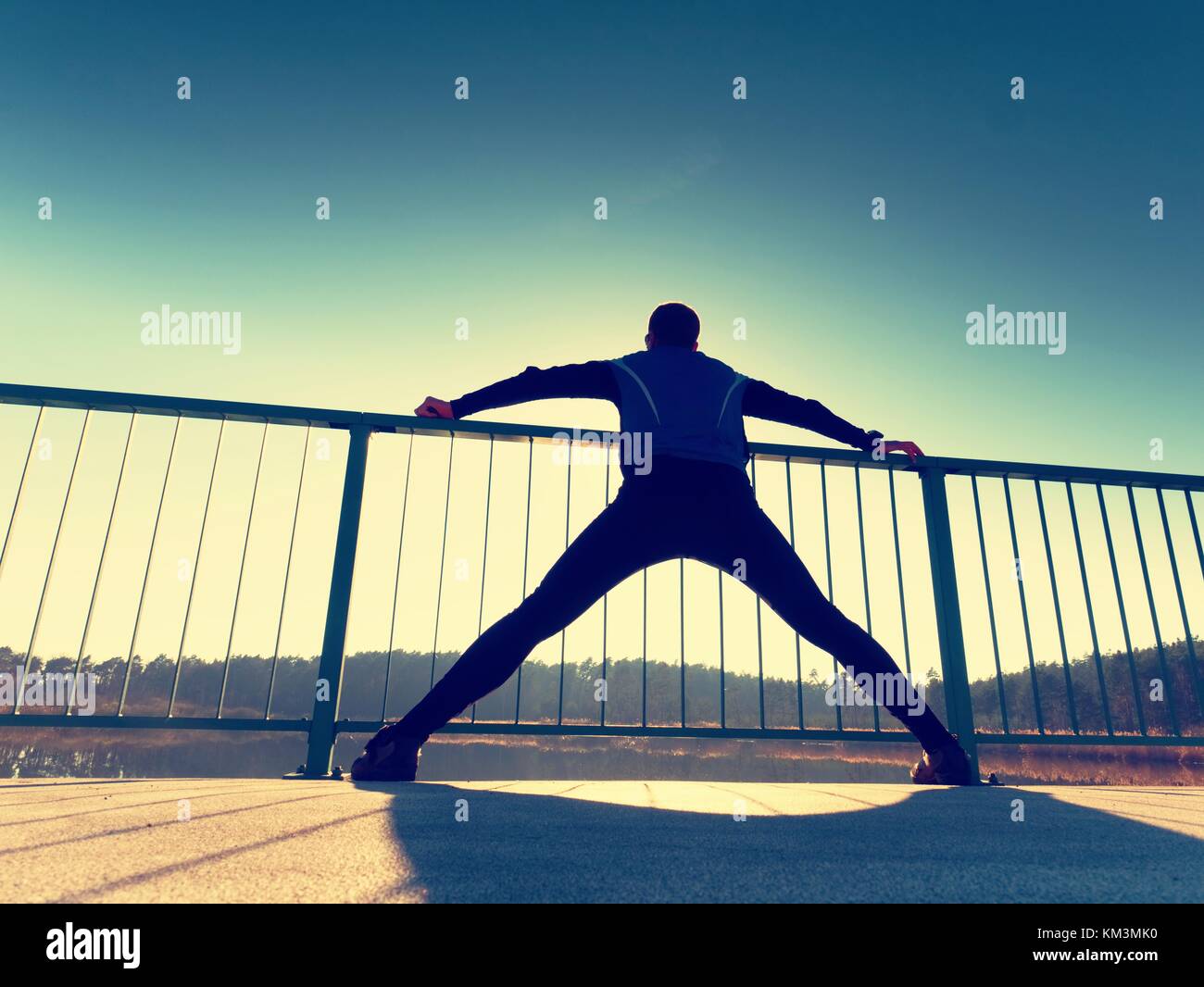 Morning runner in tall black leggings makes body stretching on bridge ...