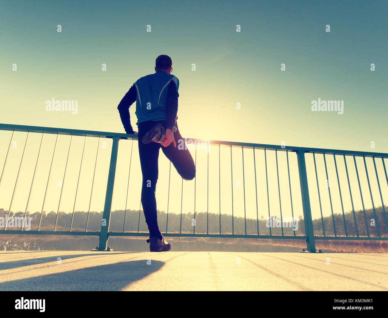The runner in tall black leggings makes body stretching on bridge path ...