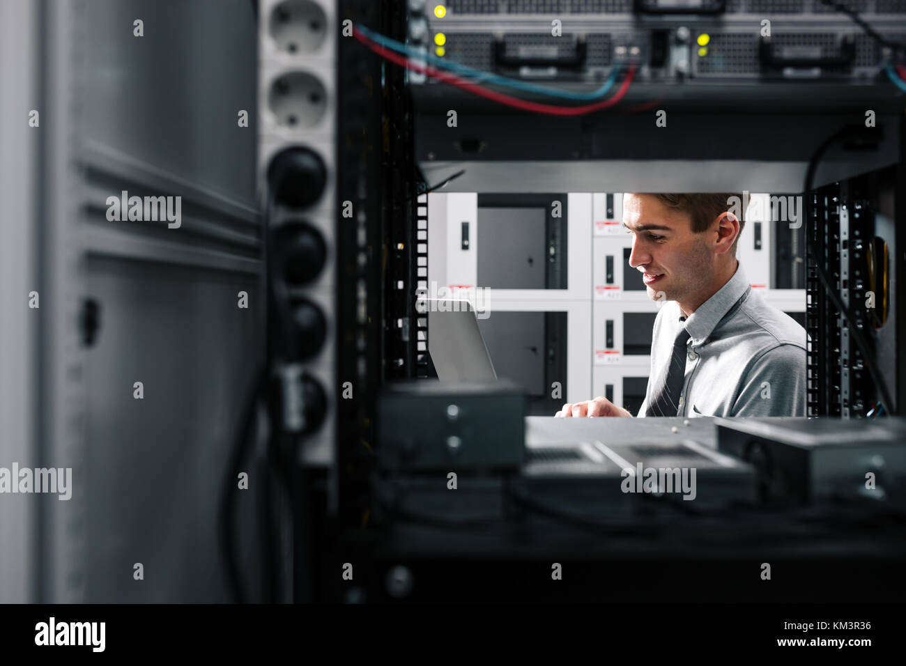 Portrait of modern young man holding laptop standing in server room ...