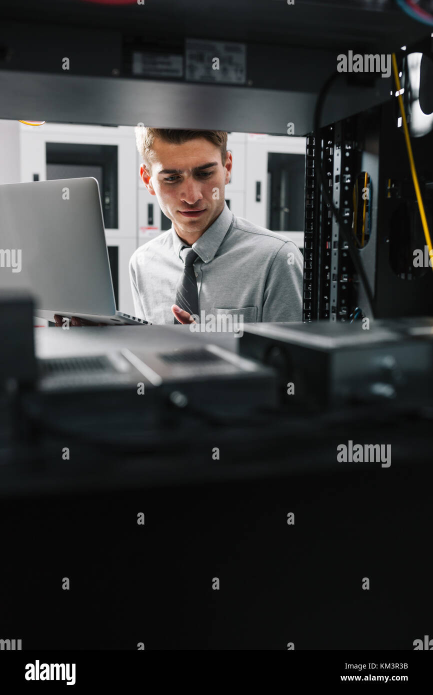 Portrait of modern young man holding laptop standing in server room ...
