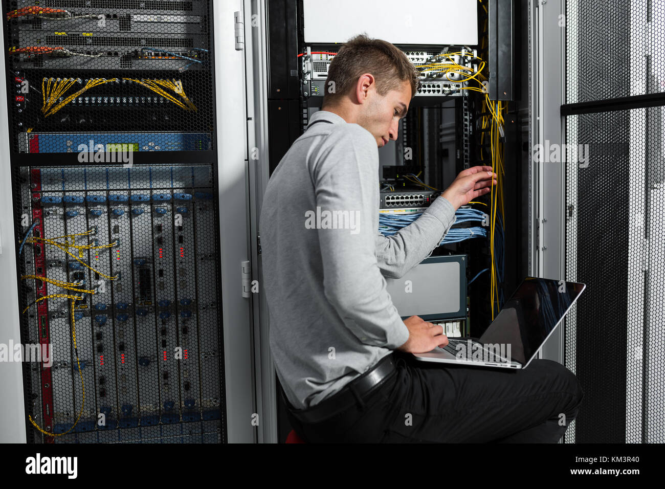 Portrait of modern young man holding laptop standing in server room ...