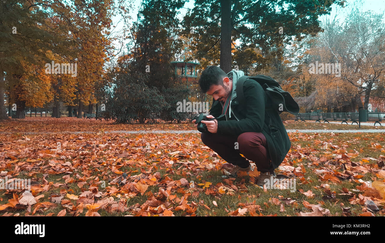 man sitting and looking photos at a dslr camera after an autumn scenery ...