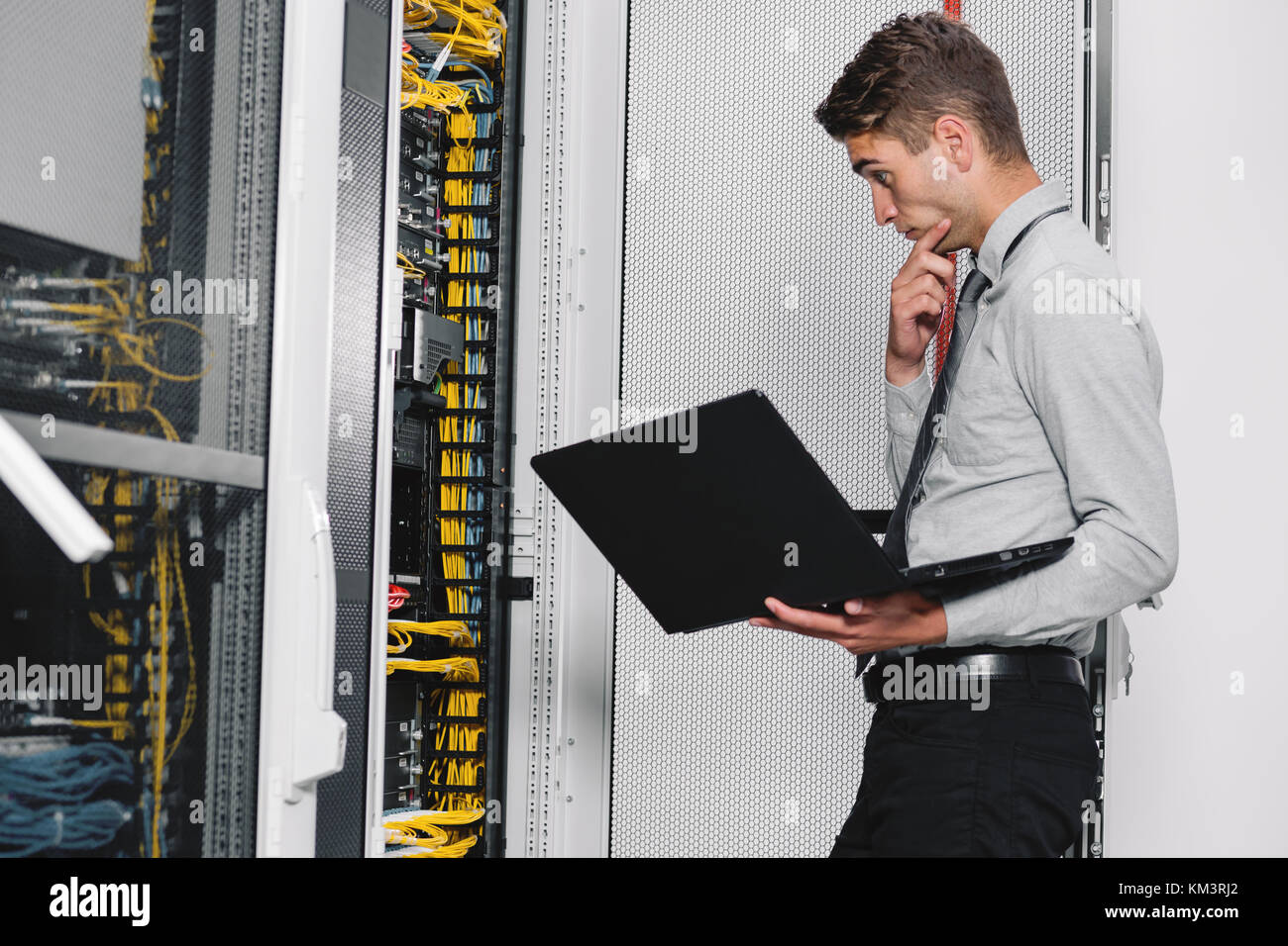 Portrait of modern young man holding laptop standing in server room ...
