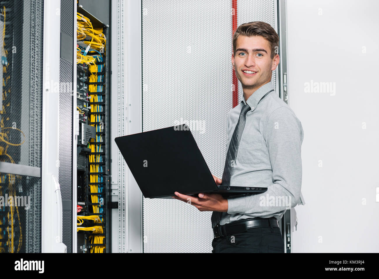 Portrait of modern young man holding laptop standing in server room ...