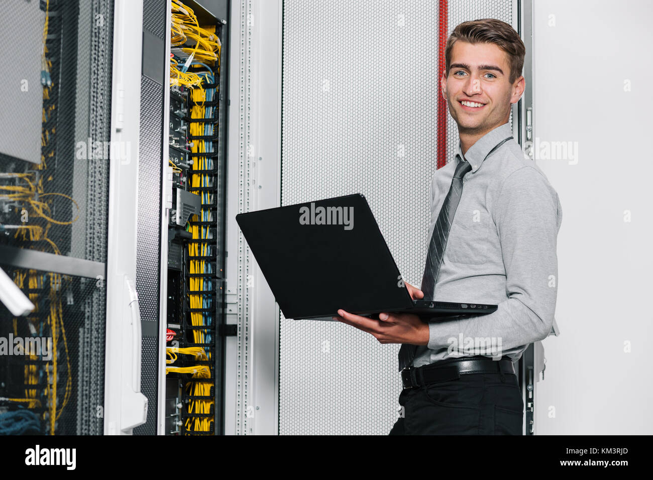 Portrait of modern young man holding laptop standing in server room ...