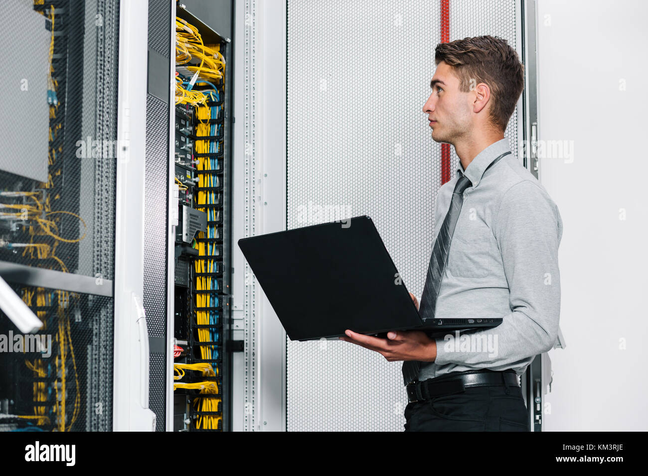 Portrait of modern young man holding laptop standing in server room ...