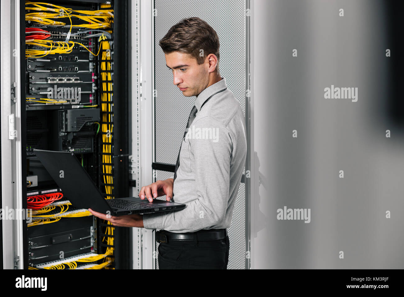 Portrait of modern young man holding laptop standing in server room ...