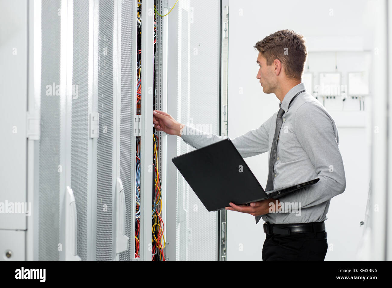 Portrait of modern young man holding laptop standing in server room ...