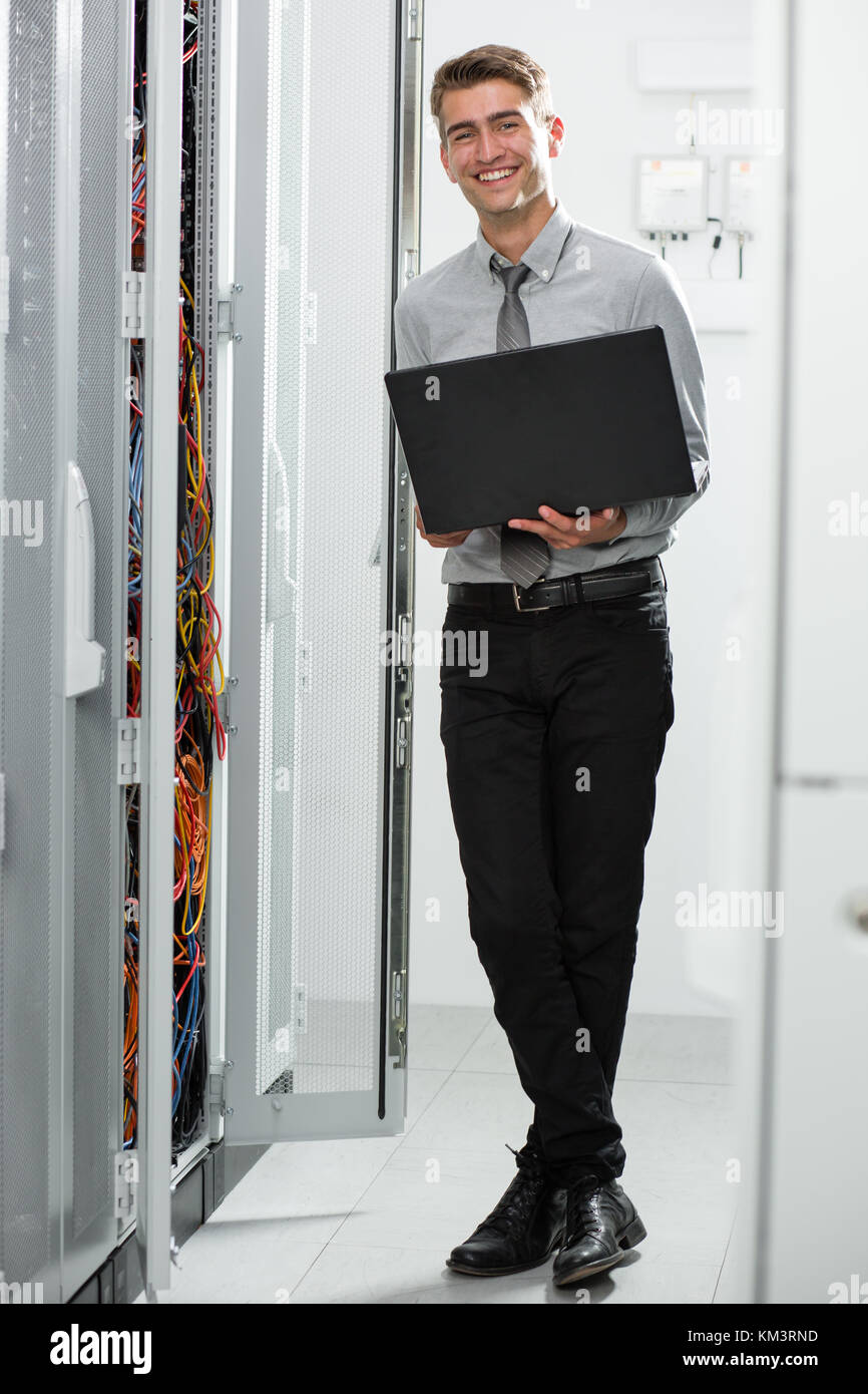 Portrait of modern young man holding laptop standing in server room ...