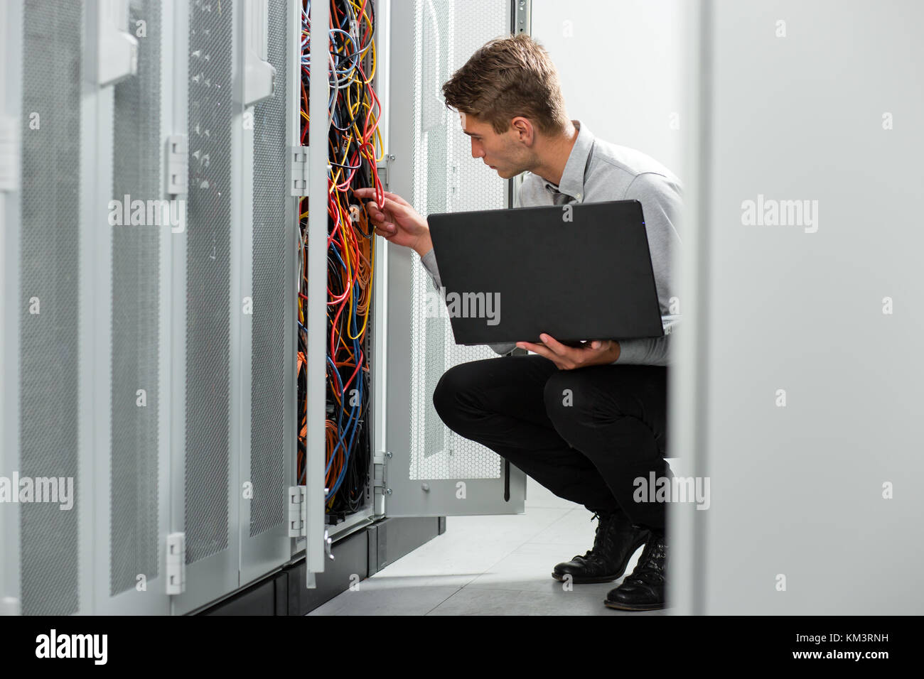 Portrait of modern young man holding laptop standing in server room ...