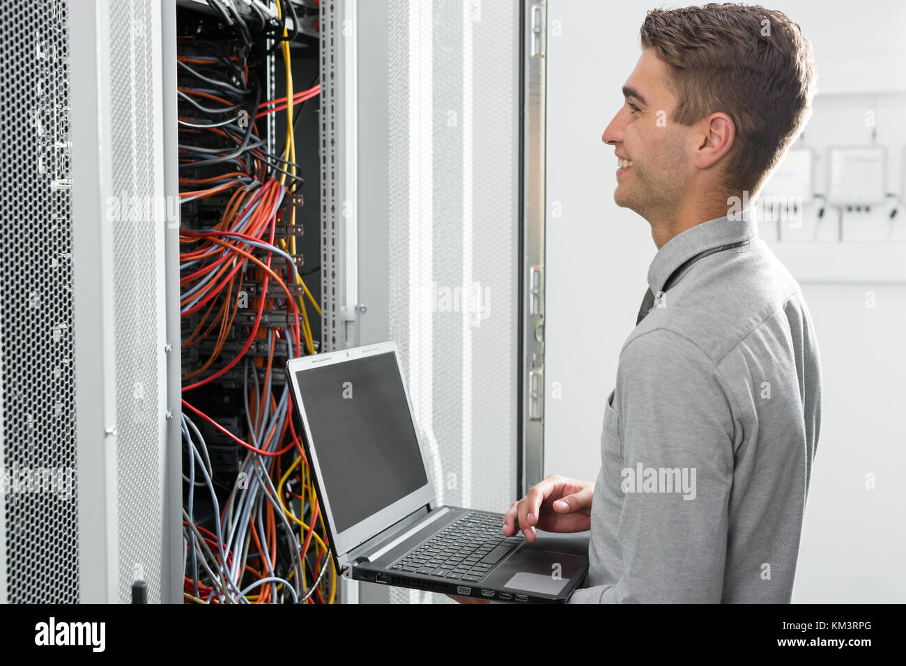 Portrait of modern young man holding laptop standing in server room ...