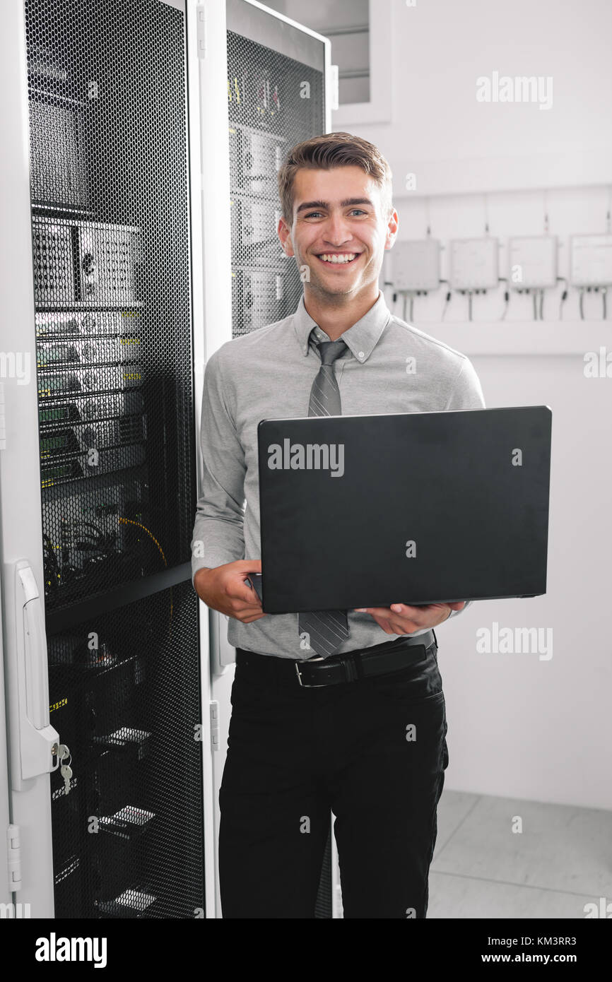 Portrait of modern young man holding laptop standing in server room ...