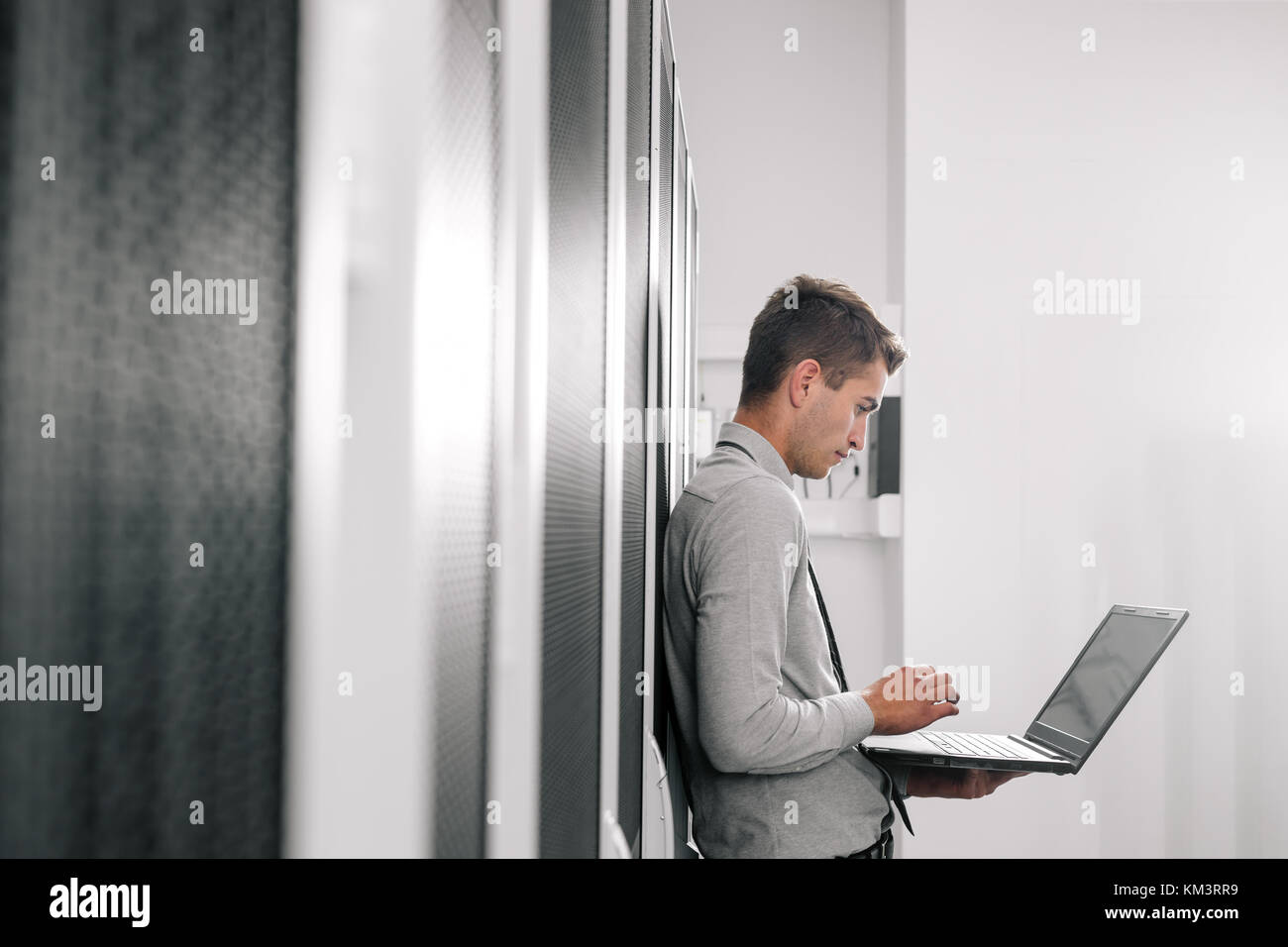 Portrait of modern young man holding laptop standing in server room ...