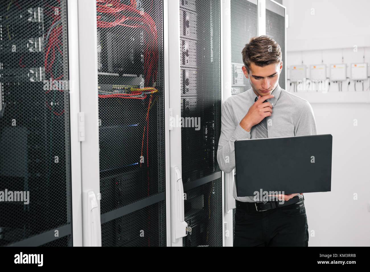 Portrait of modern young man holding laptop standing in server room ...