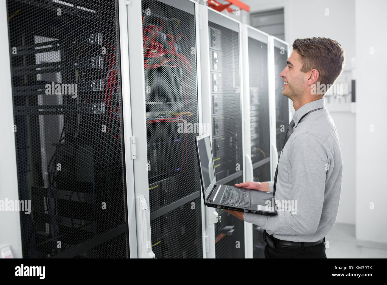 Portrait of modern young man holding laptop standing in server room ...