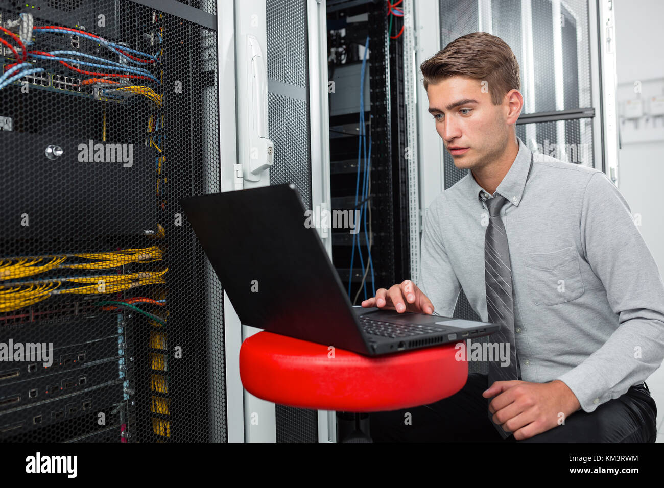 Portrait of modern young man holding laptop standing in server room ...