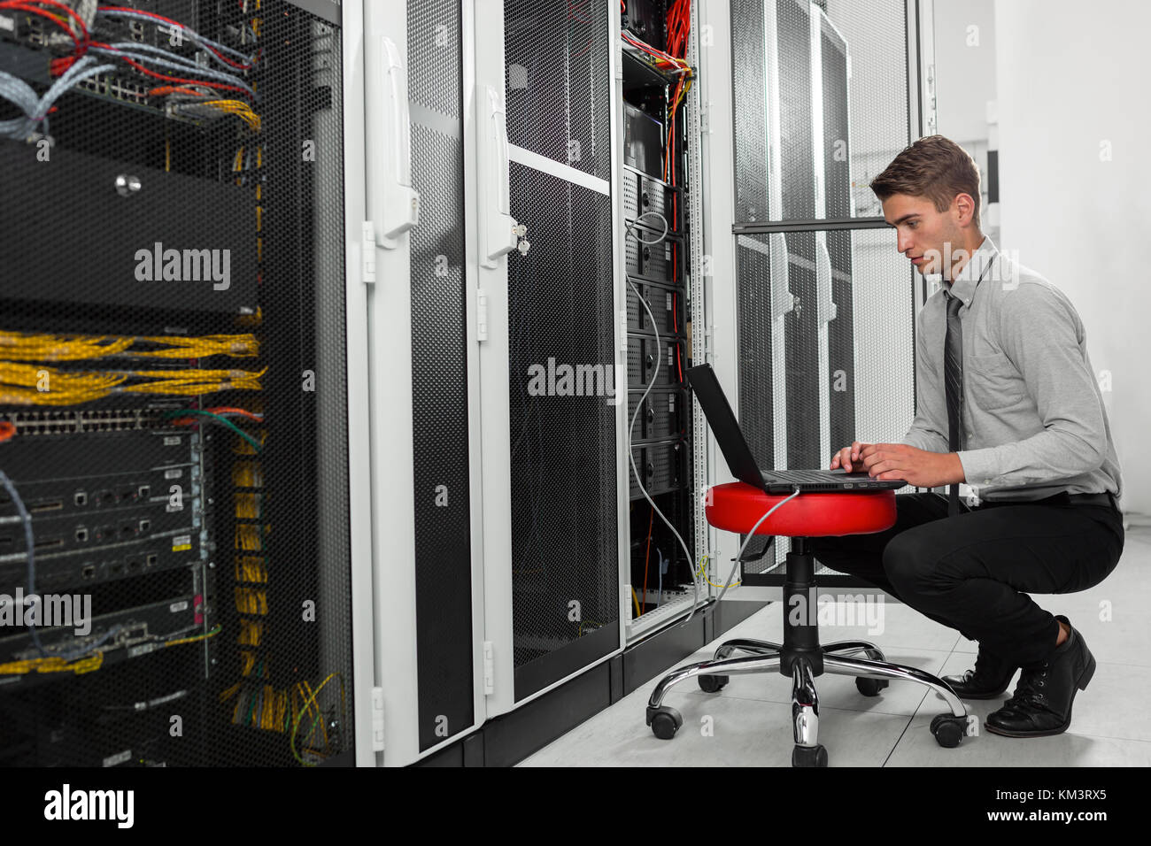 Portrait of modern young man holding laptop standing in server room ...