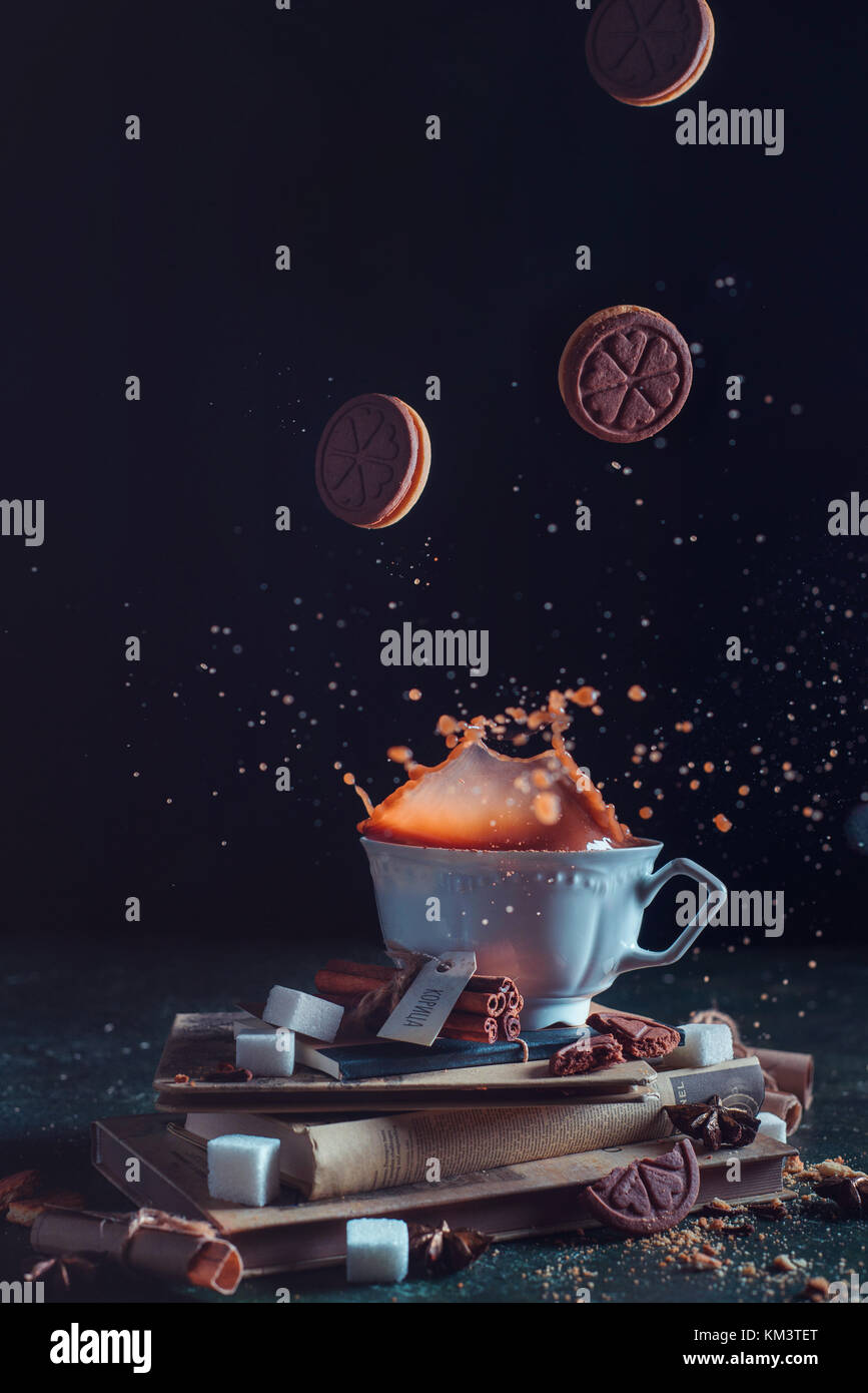 Porcelain tea cup with falling cookies and a splash on a dark ...