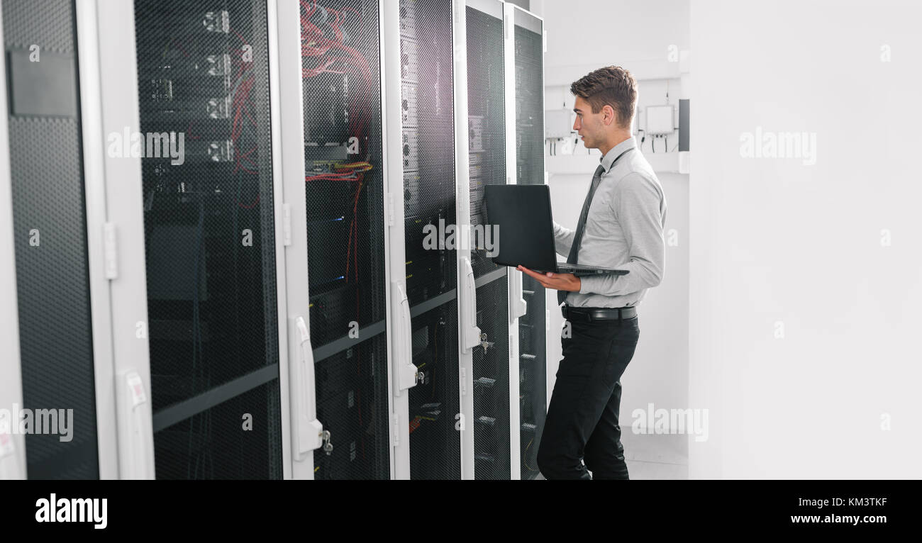 Portrait of modern young man holding laptop standing in server room ...
