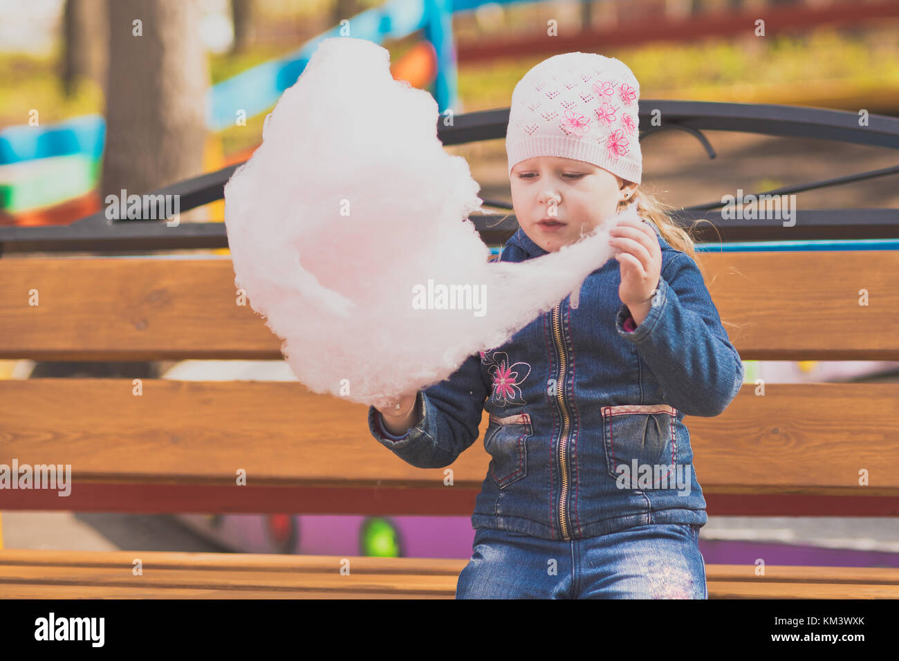 Little girl on a Park bench eating cotton candy. Portrait of a girl in ...