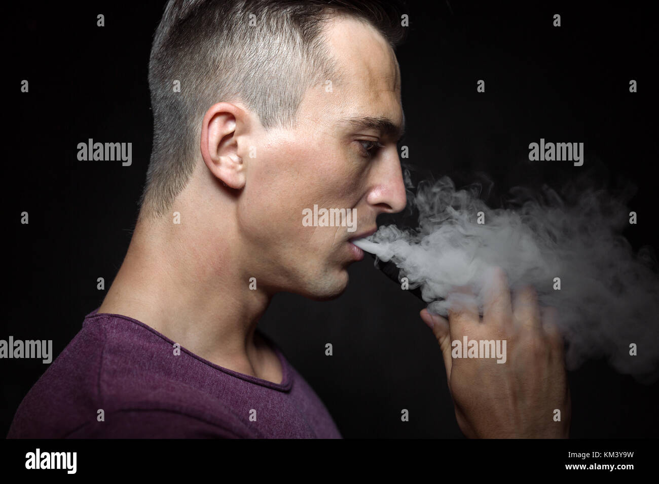 Man on black background vaping and releasing a cloud Stock Photo - Alamy