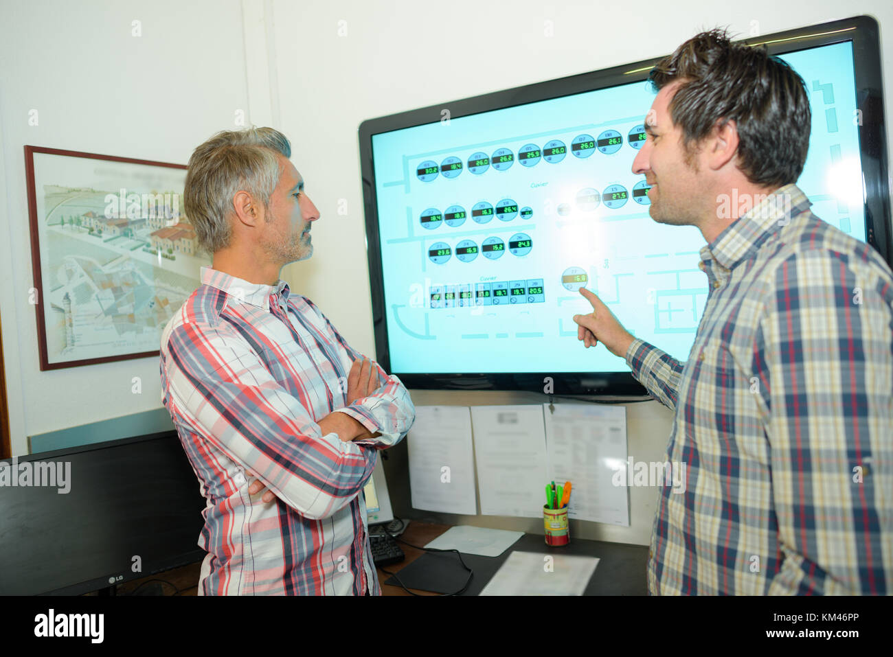 Two men looking at wide screen mounted on wall Stock Photo - Alamy
