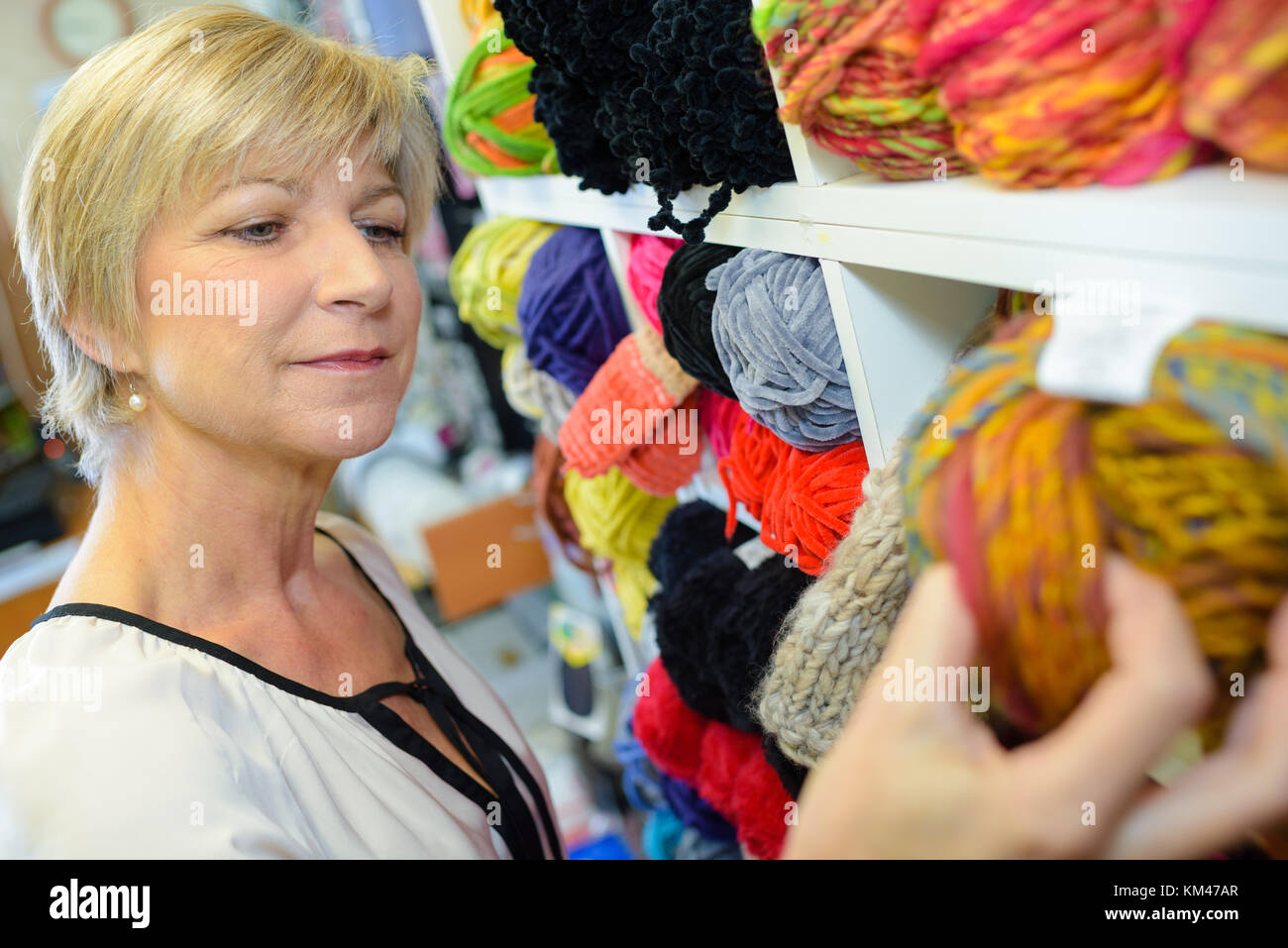 mature smiling blonde woman customer choosing multicolored spool with ...