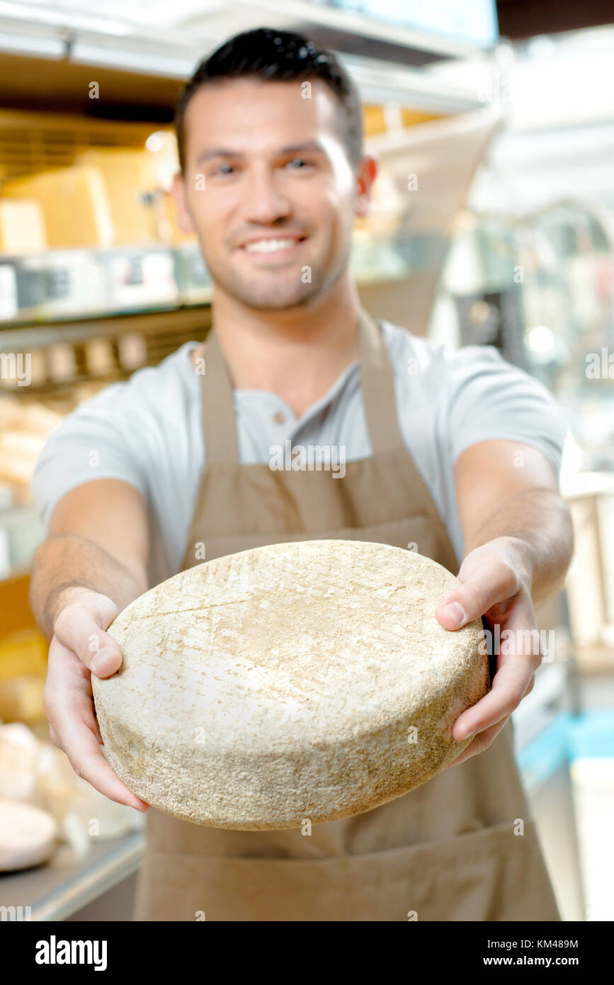 Shop worker holding circular cheese in outstretched arms Stock Photo ...
