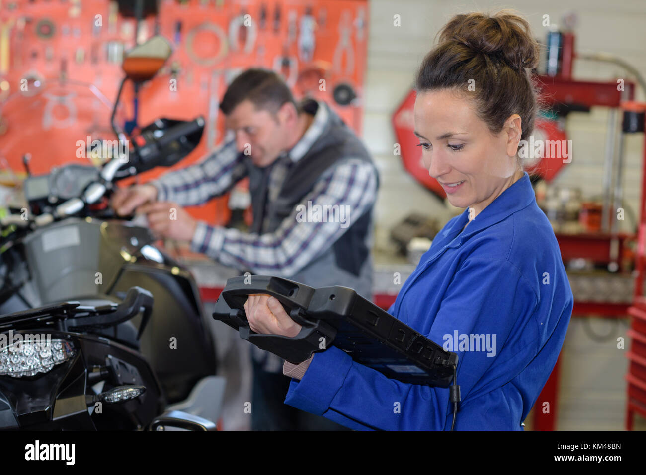 Woman holding computerised device in motorcycle garage Stock Photo - Alamy
