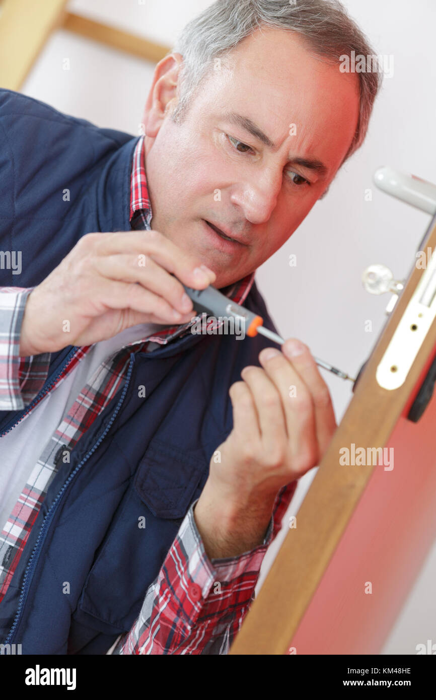Senior man screwing lock into door Stock Photo - Alamy