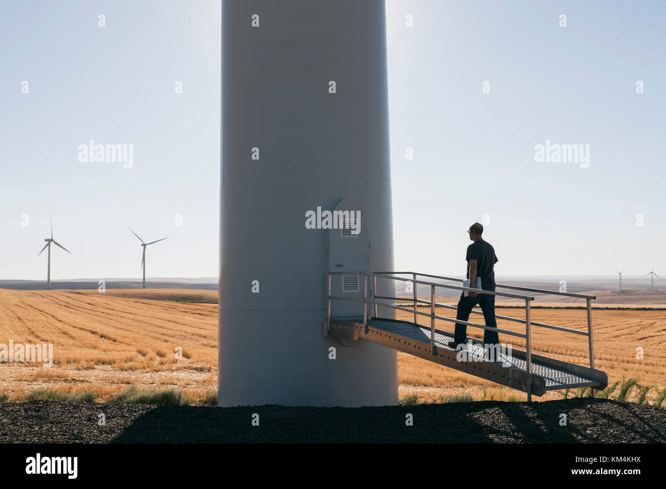 A wind farm technician standing and using a laptop at the base of a ...