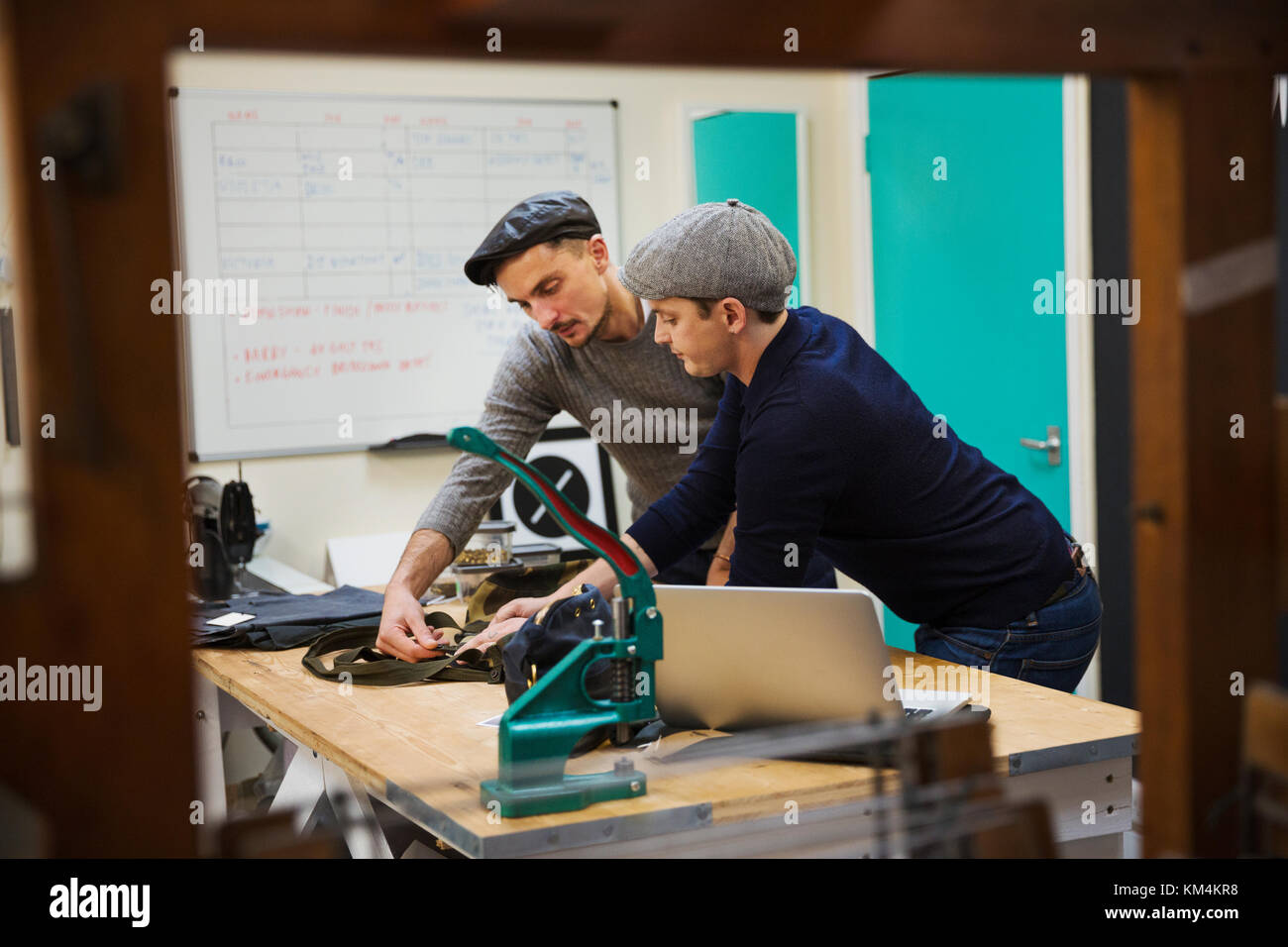 Two men, tailors leaning over a workbench discussing a project ...
