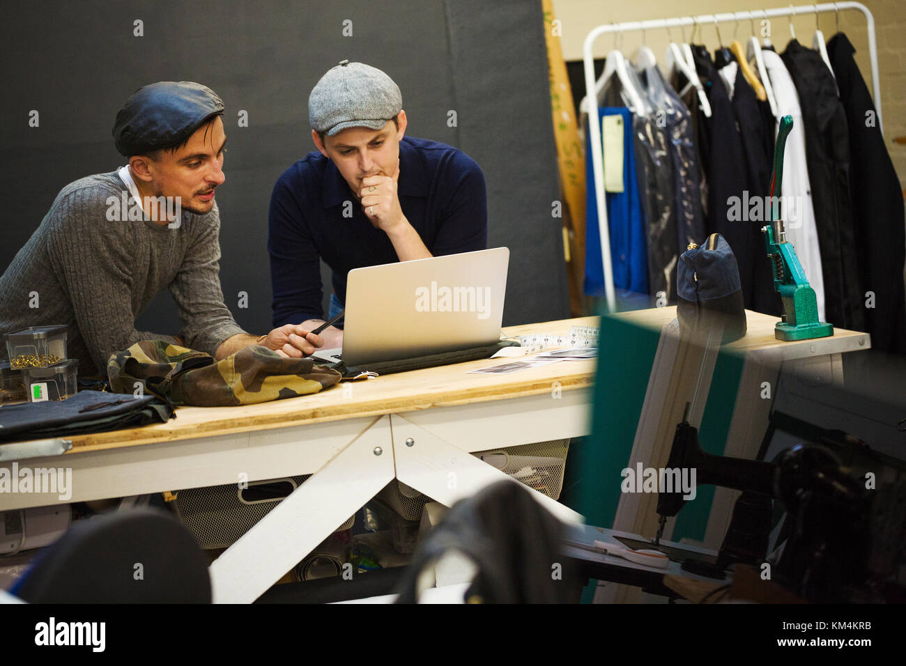 Two men working at a laptop, sharing the screen. A tailoring workshop ...