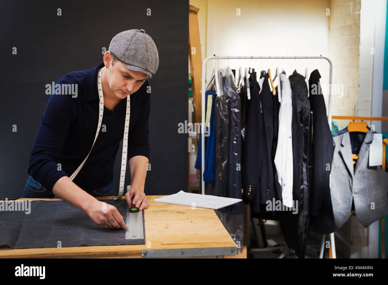 A man at a workbench measuring and marking a piece of grey fabric with ...