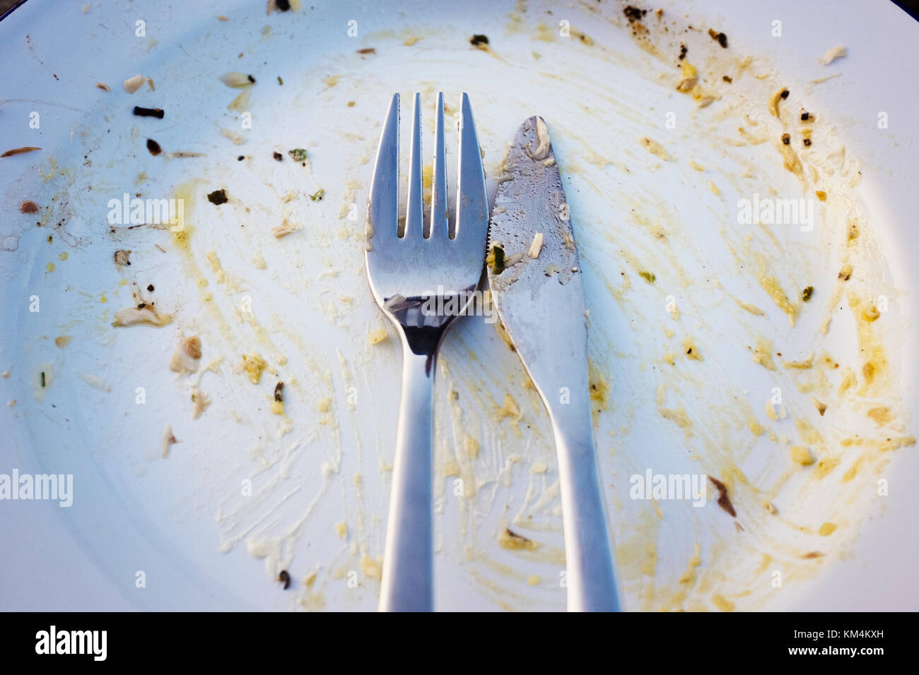 An empty plate after a meal, scraps of food and knife and fork placed ...