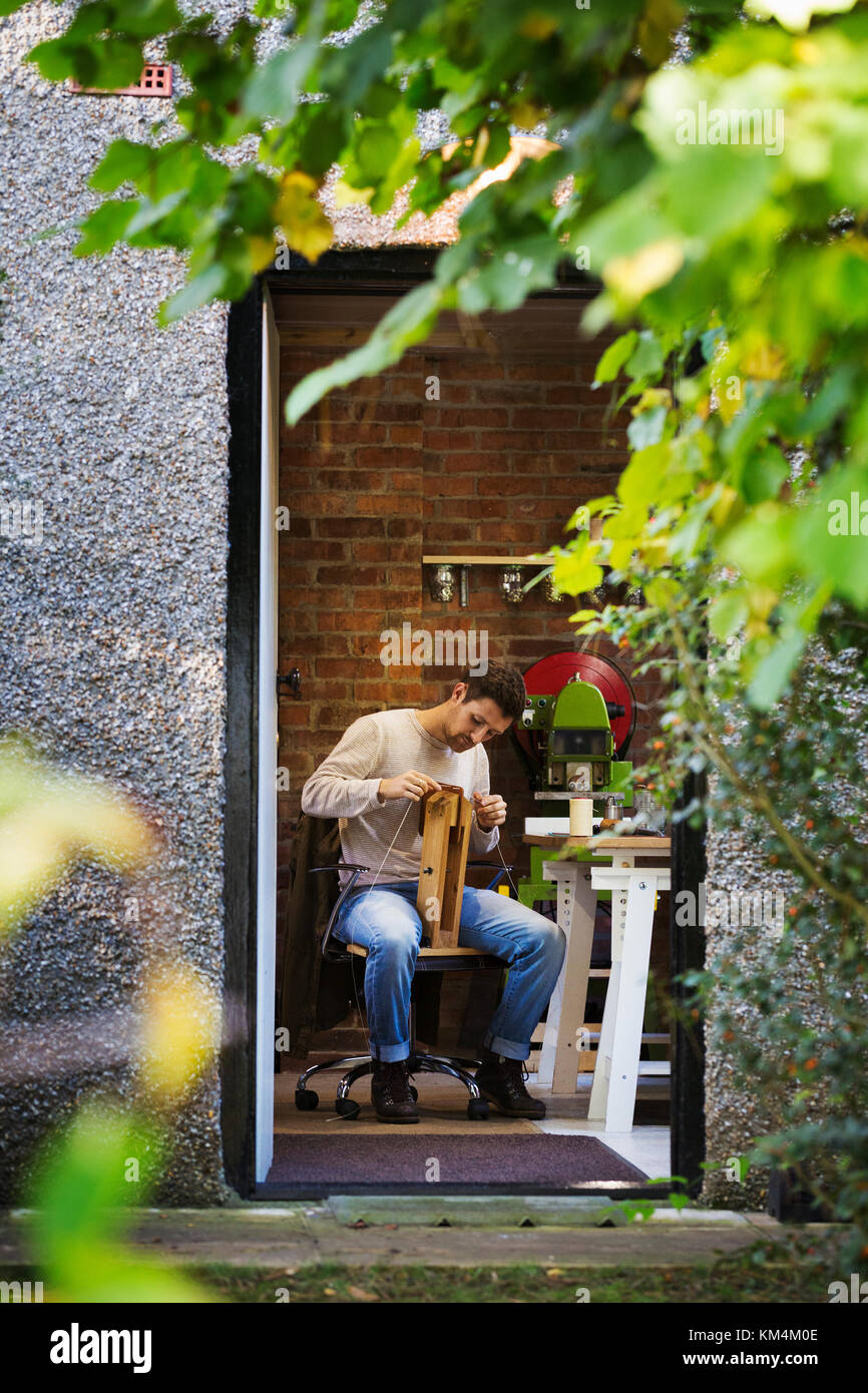 View through an open door of a craftsman leatherworker seated in his ...