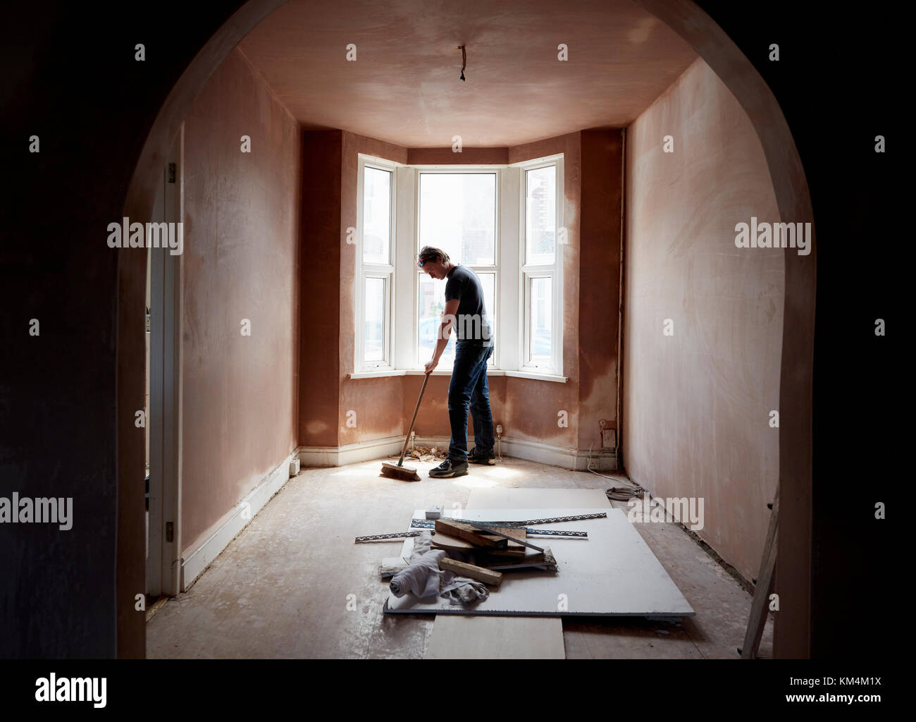 A builder sweeping and tidying up in a renovated replastered house with ...