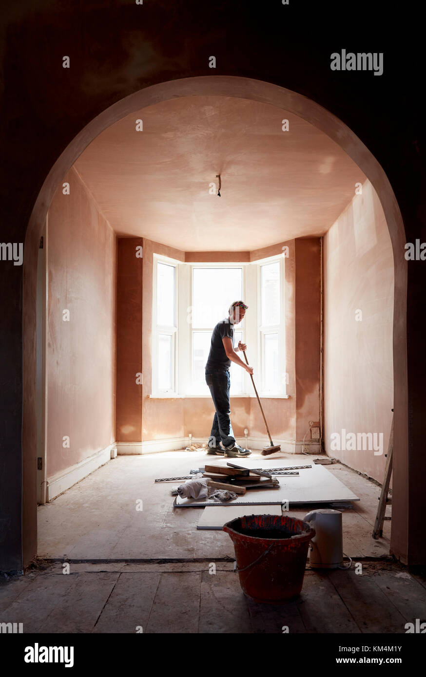 A builder sweeping and tidying up in a renovated replastered house with ...