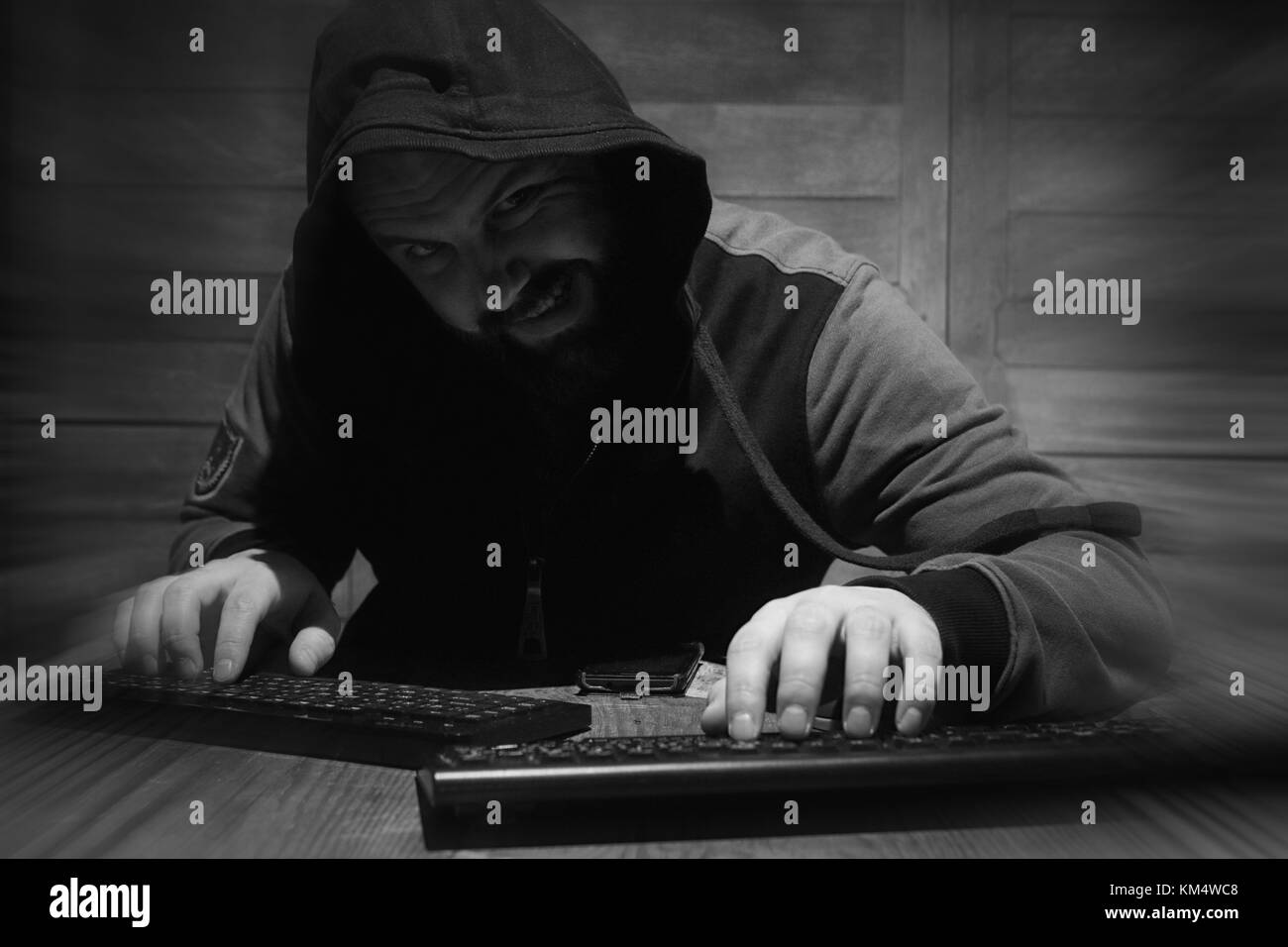 The hacker in the hood sits and works behind the computer Stock Photo ...